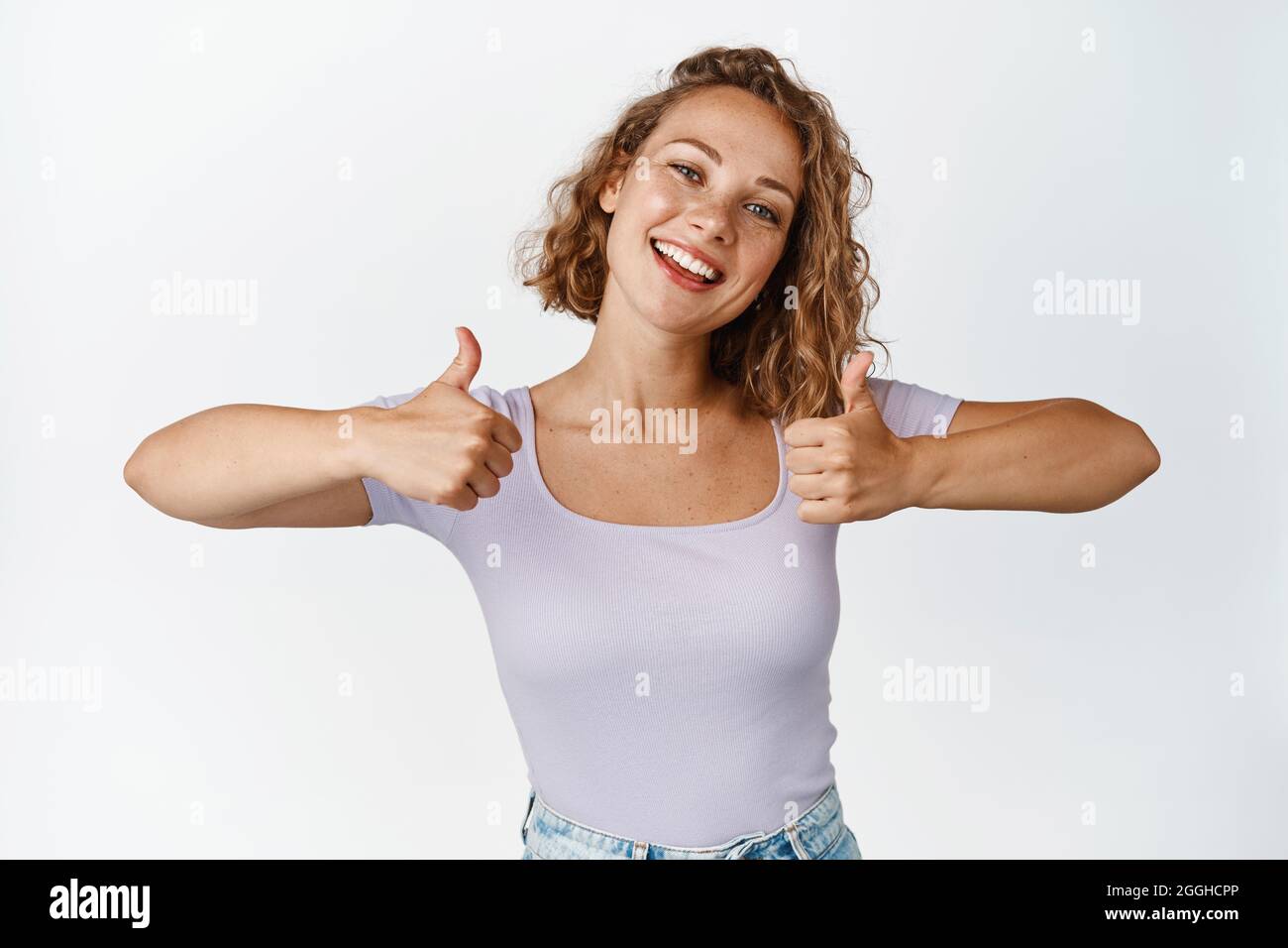 Happy blond woman shows thumbs up and smiles pleased, praise something ...