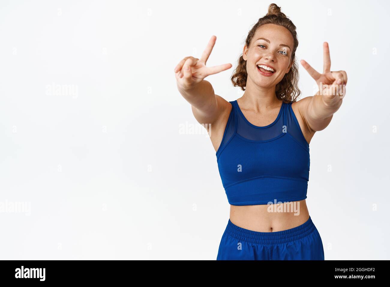 Happy and healthy sportswoman shows peace v-sign and smiling, wearing ...