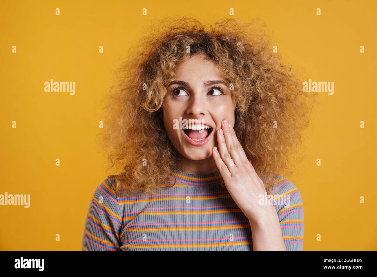 Happy smiling young blonde woman with fizzy hair in casual clothes standing over yellow wall ...