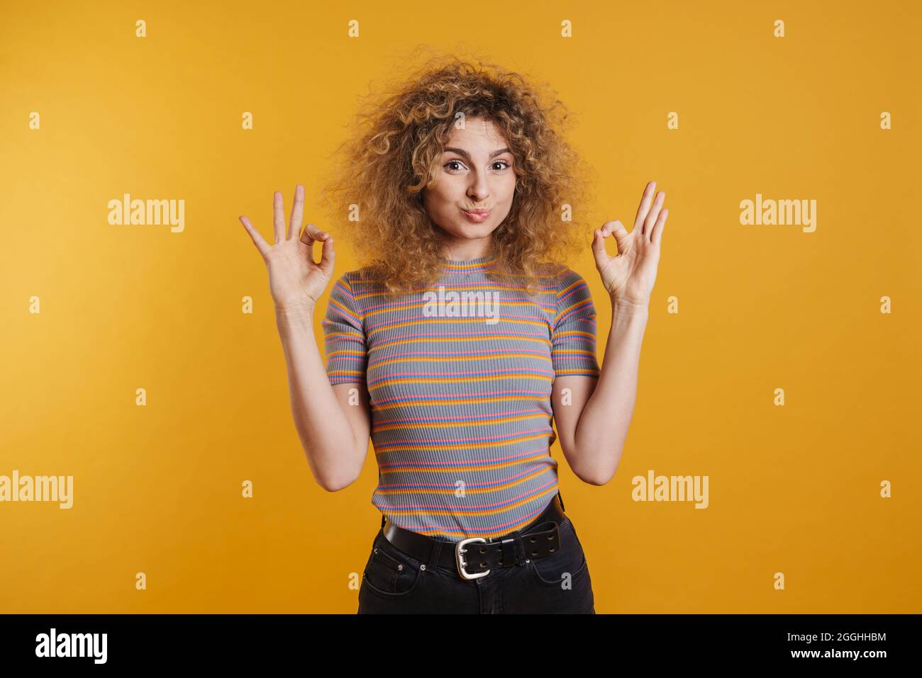 Happy smiling young blonde woman with fizzy hair in casual clothes standing over yellow wall ...