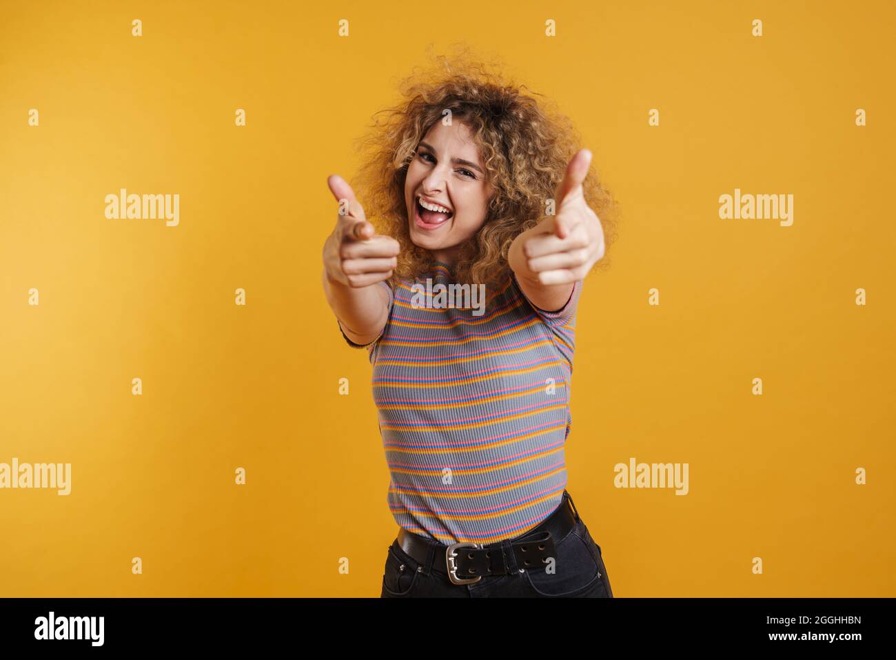Happy excited young blonde woman with fizzy hair in casual clothes standing over yellow wall ...