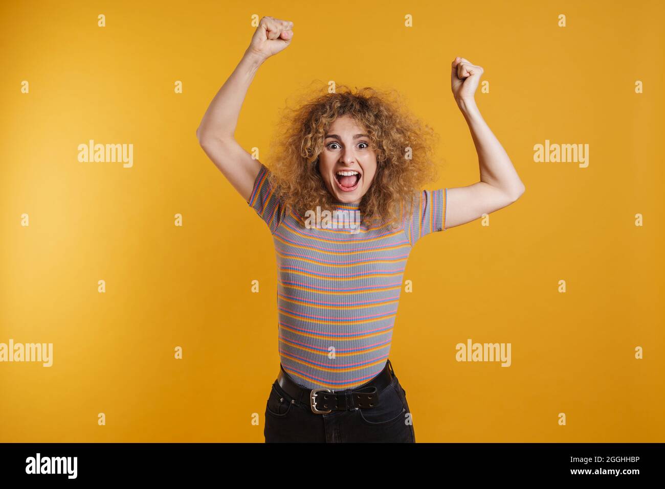 Happy smiling young blonde woman with fizzy hair in casual clothes standing over yellow wall ...