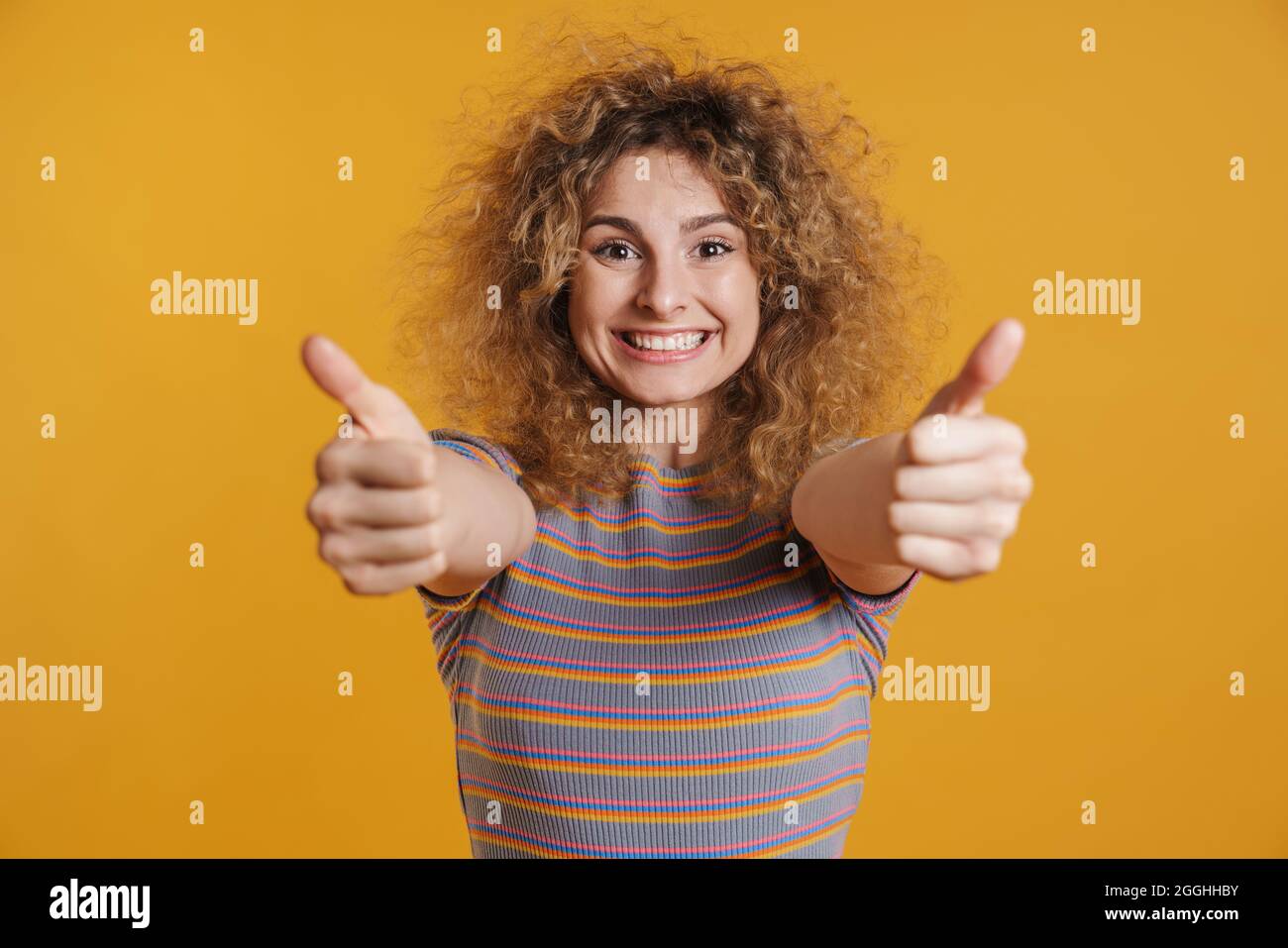 Happy excited young casual woman with fizzy hairstyle standing over yellow wall background ...