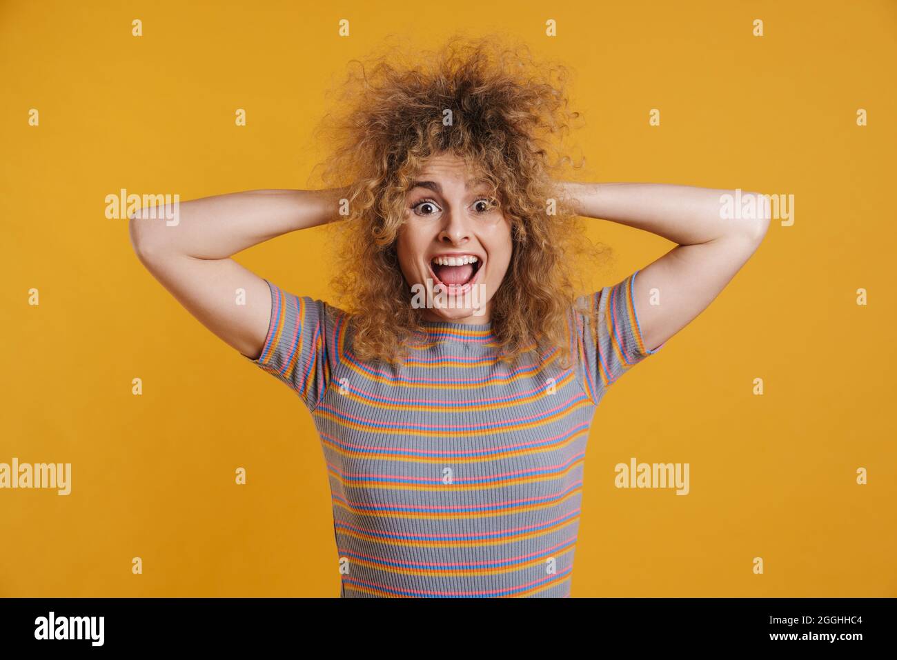 Happy smiling young blonde woman with fizzy hair in casual clothes standing over yellow wall ...