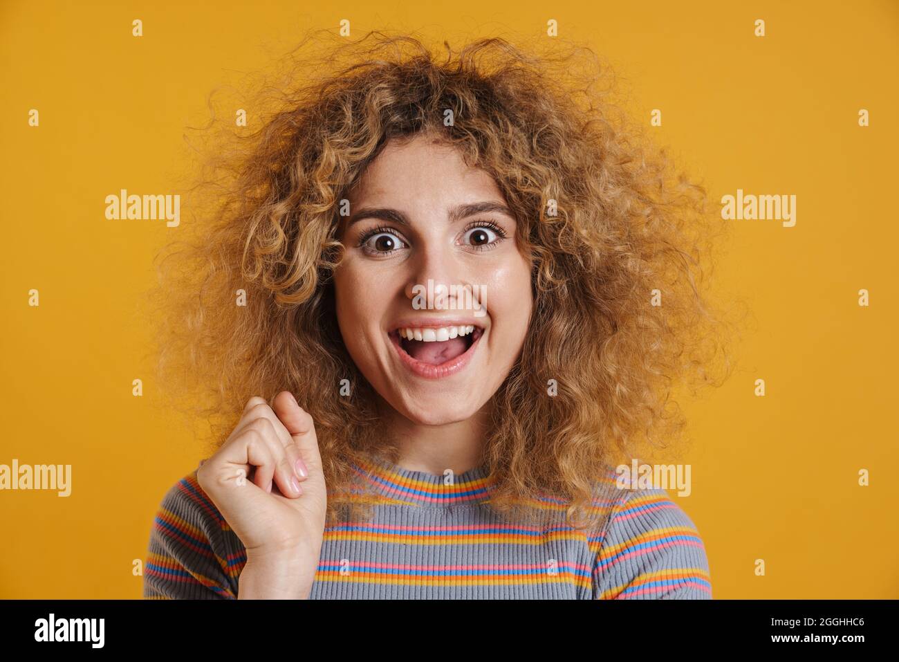 Happy smiling young blonde woman with fizzy hair in casual clothes standing over yellow wall ...