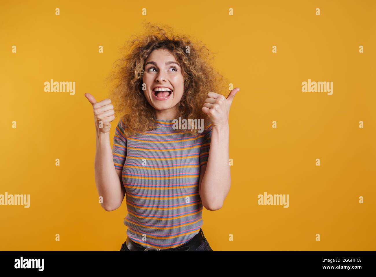Happy excited young casual woman with fizzy hairstyle standing over yellow wall background ...