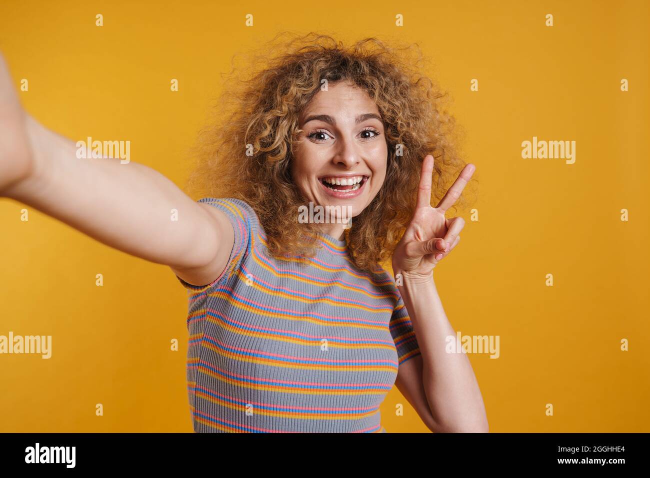 Happy smiling young blonde woman with fizzy hair in casual clothes standing over yellow wall ...