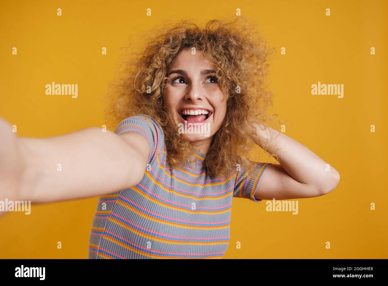 Happy excited young casual woman with fizzy hairstyle standing over yellow wall background ...