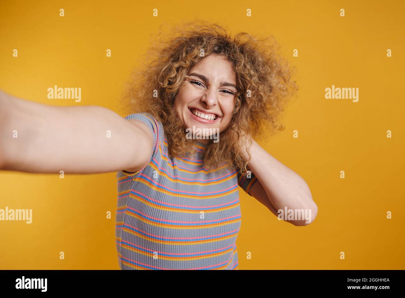 Happy excited young casual woman with fizzy hairstyle standing over yellow wall background ...