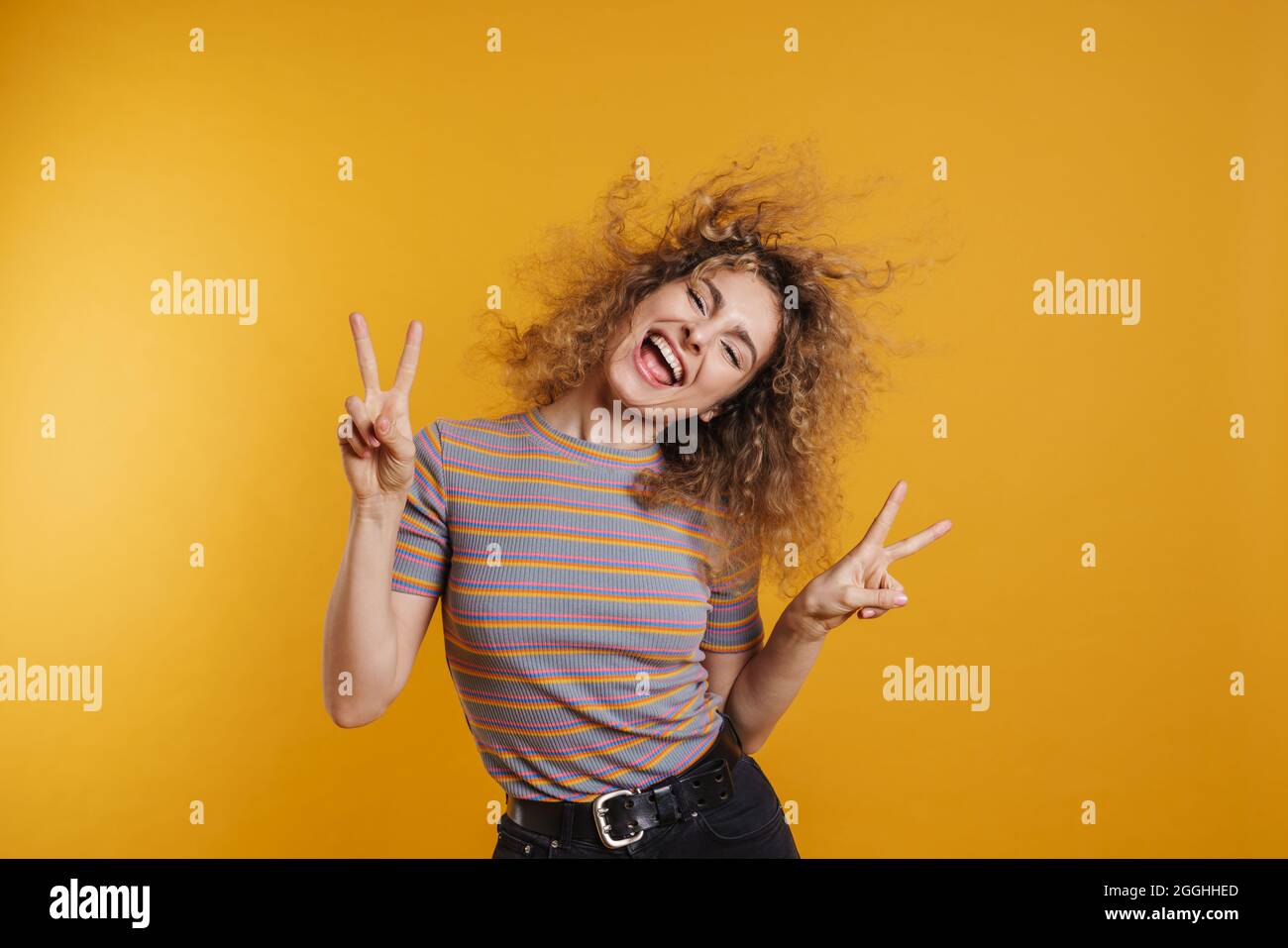 Happy excited young casual woman with fizzy hairstyle standing over yellow wall background ...