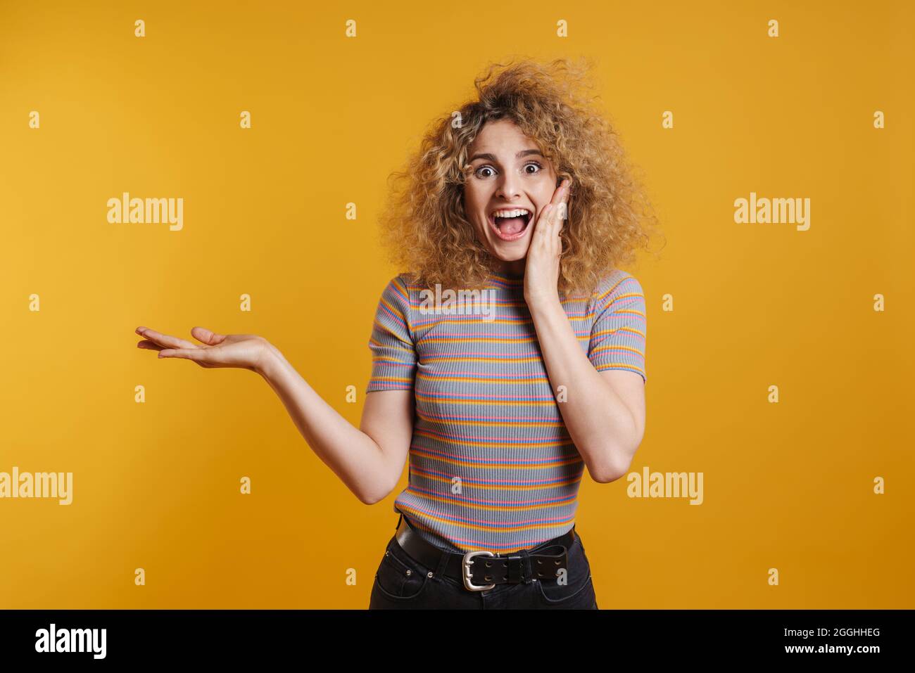 Happy excited young blonde woman with fizzy hair in casual clothes standing over yellow wall ...