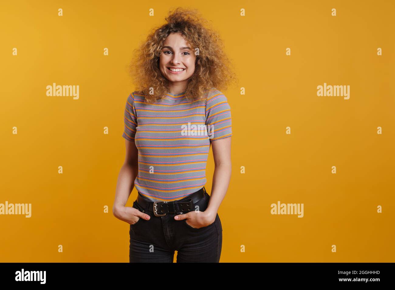 Happy smiling young blonde woman with fizzy hair in casual clothes standing over yellow wall ...