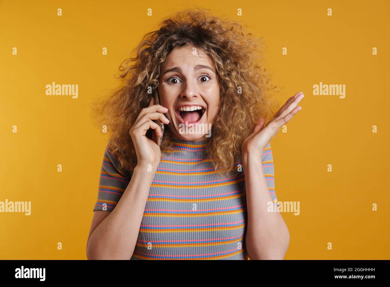 Happy smiling young blonde woman with fizzy hair in casual clothes standing over yellow wall ...