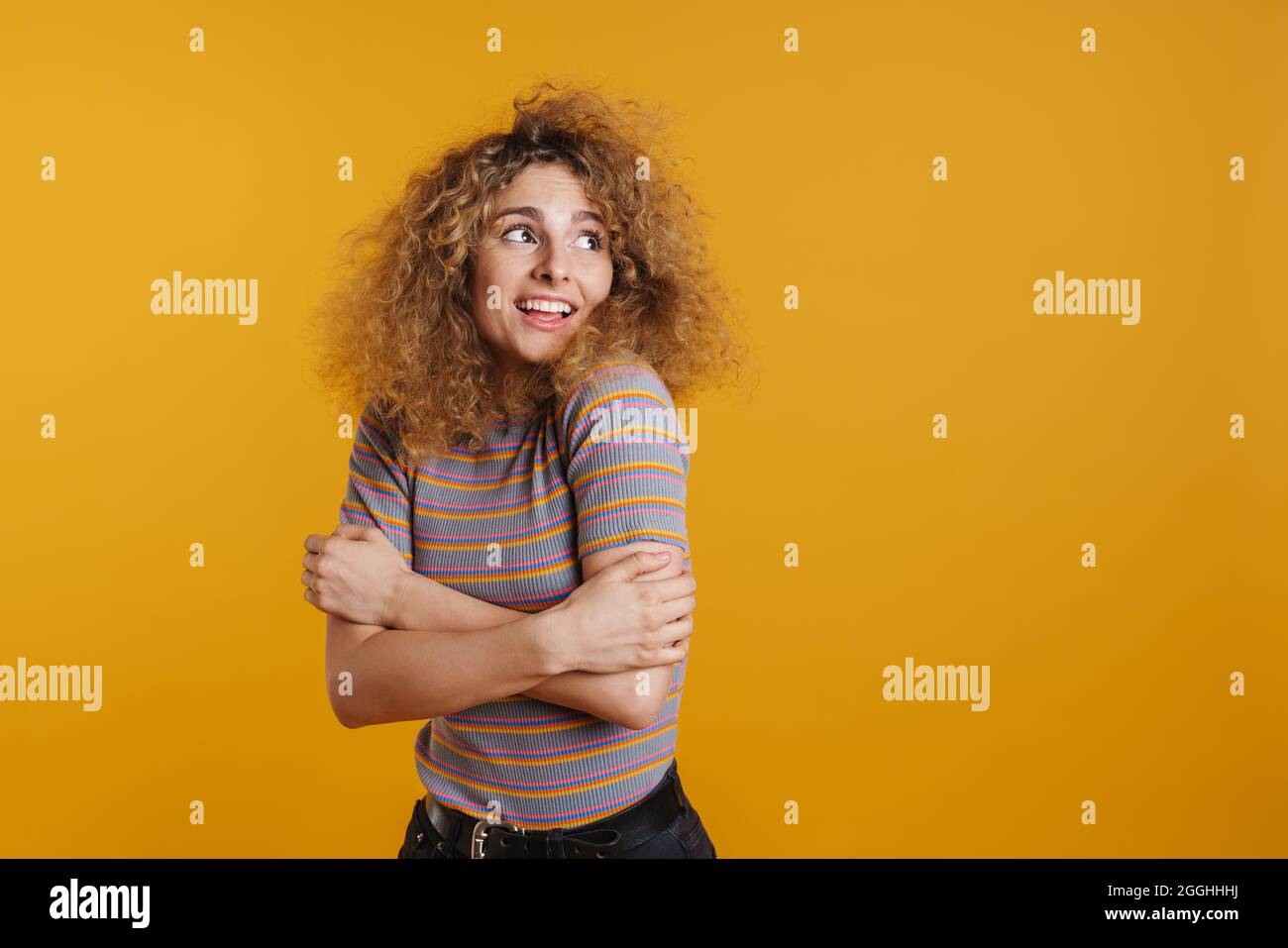 Happy smiling young blonde woman with fizzy hair in casual clothes standing over yellow wall ...