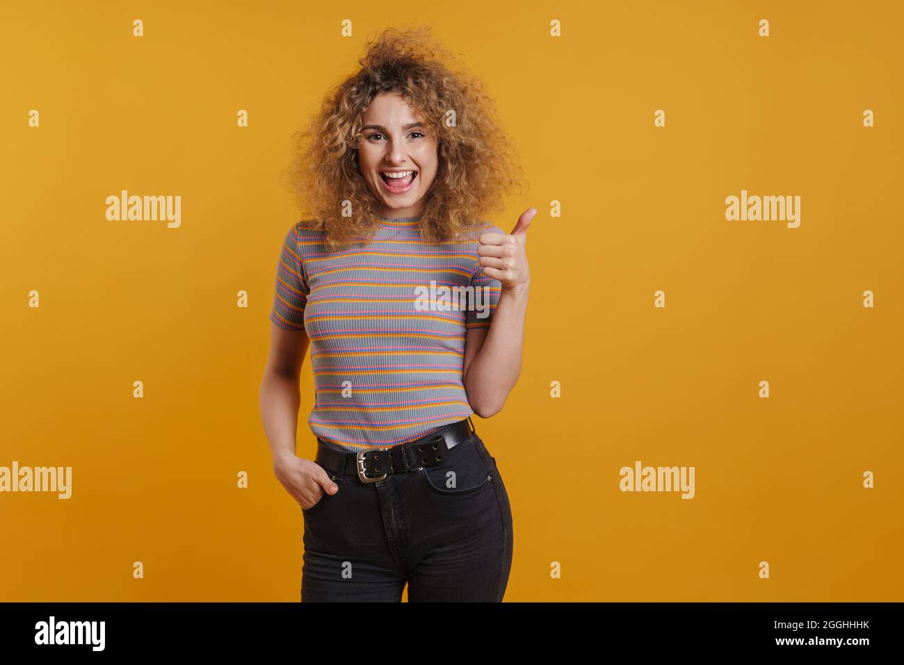 Happy smiling young blonde woman with fizzy hair in casual clothes standing over yellow wall ...