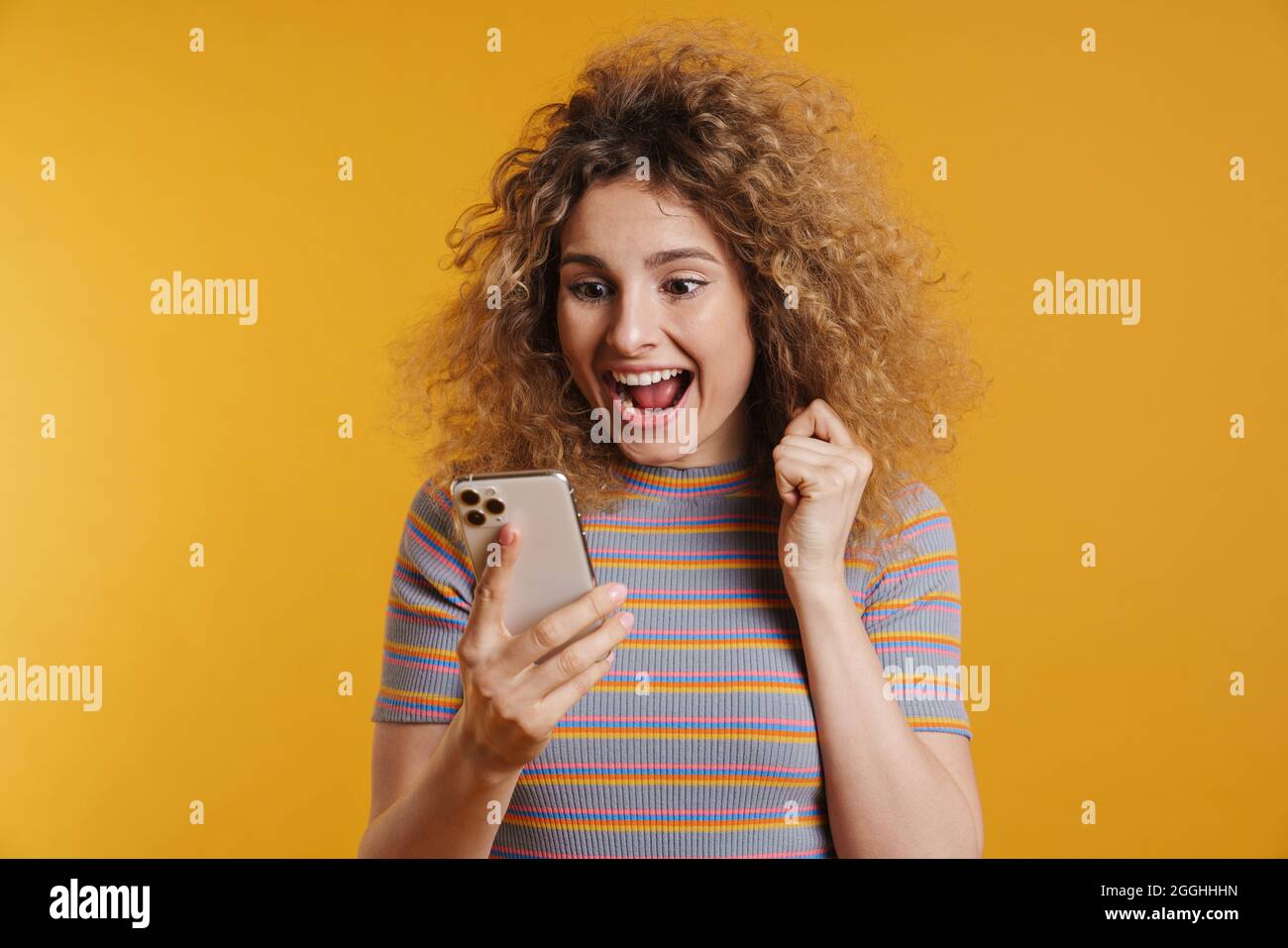 Happy smiling young blonde woman with fizzy hair in casual clothes standing over yellow wall ...
