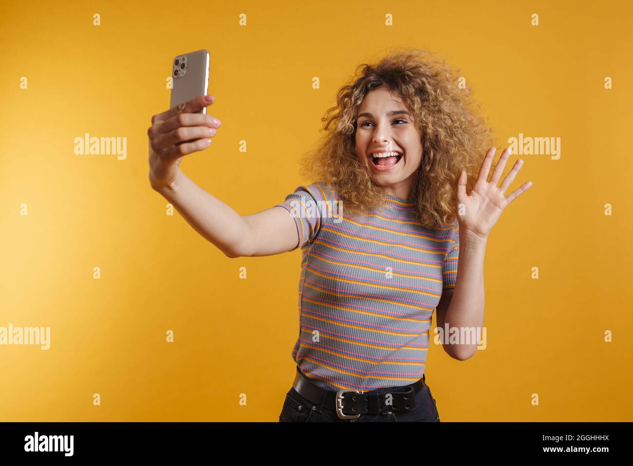Happy smiling young blonde woman with fizzy hair in casual clothes standing over yellow wall ...