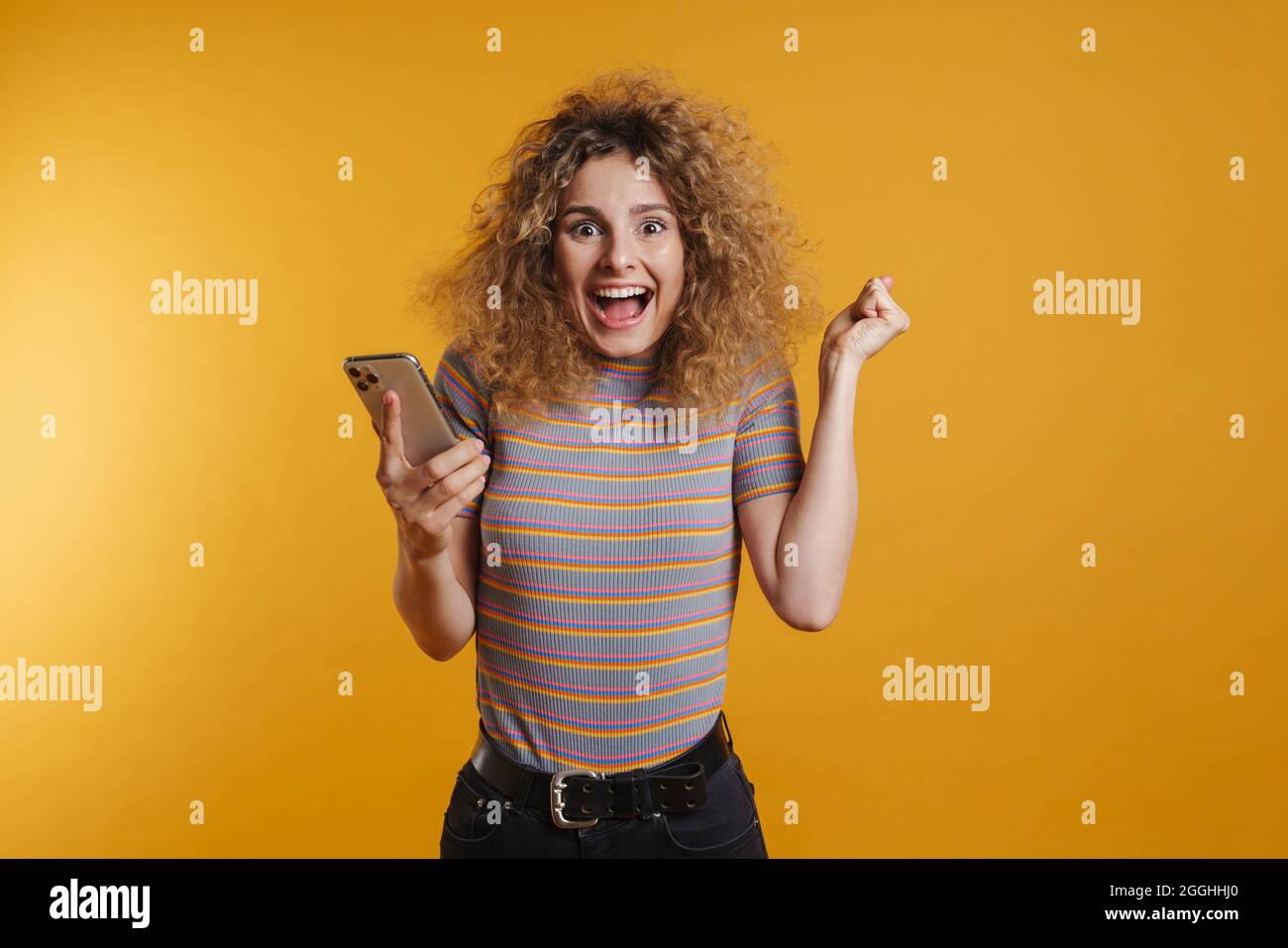 Happy smiling young blonde woman with fizzy hair in casual clothes standing over yellow wall ...