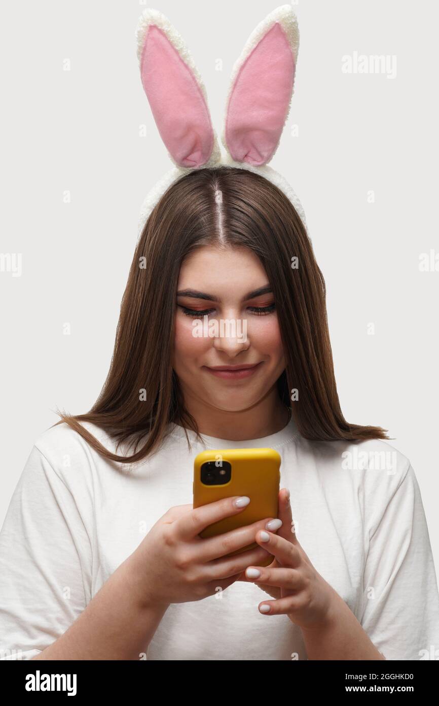 Happy smiling young woman wearing Easter bunny ears and using mobile ...