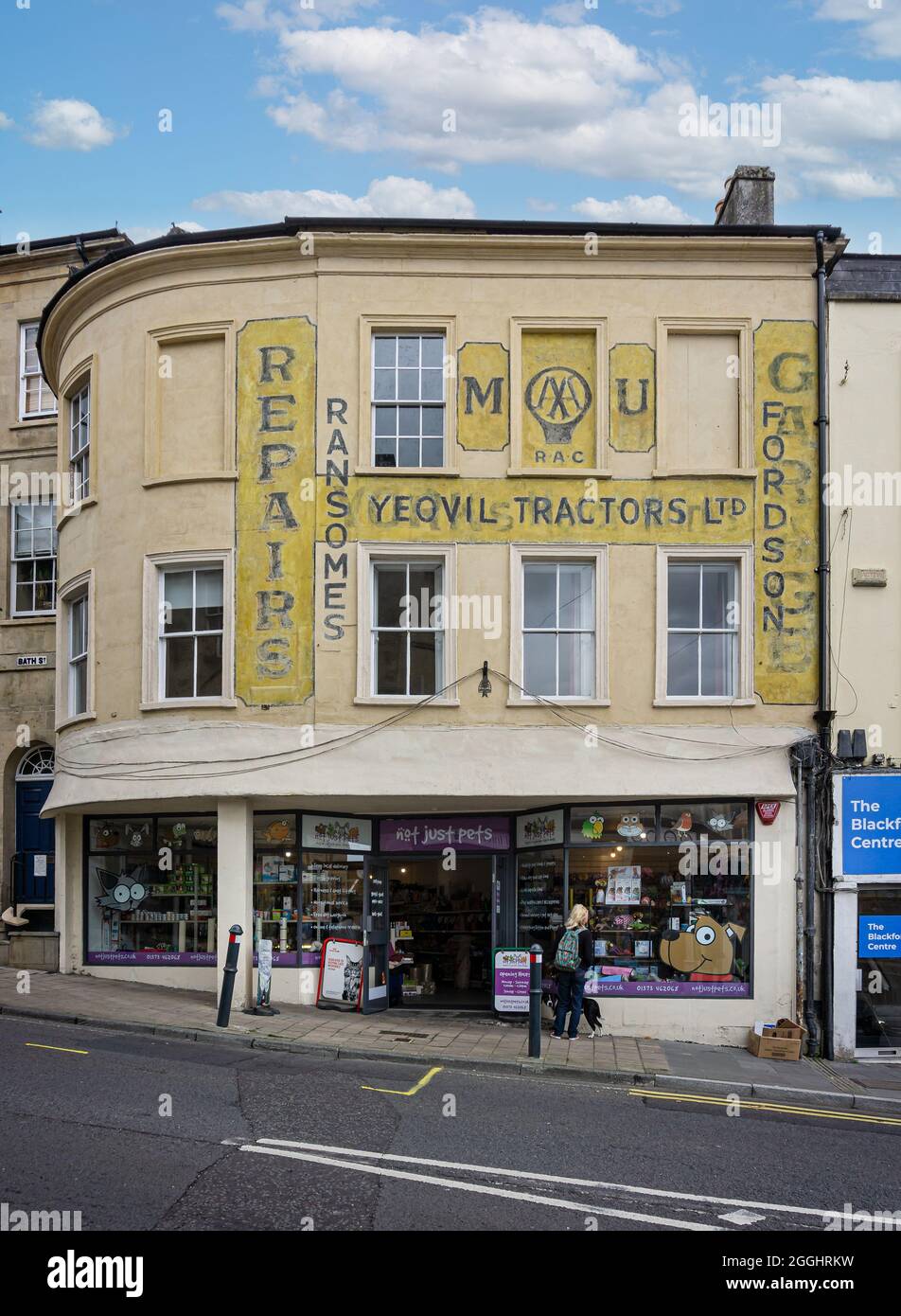 Vintage faded yellow signs for AA, tractors etc on building wall in ...