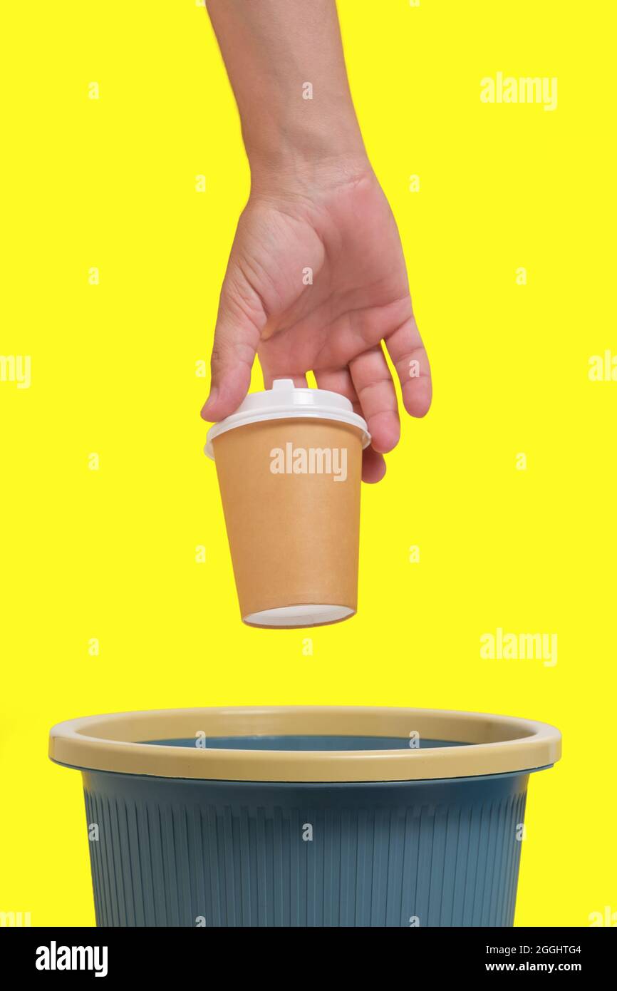 Hand on yellow background throws disposable cup of takeaway coffee into ...
