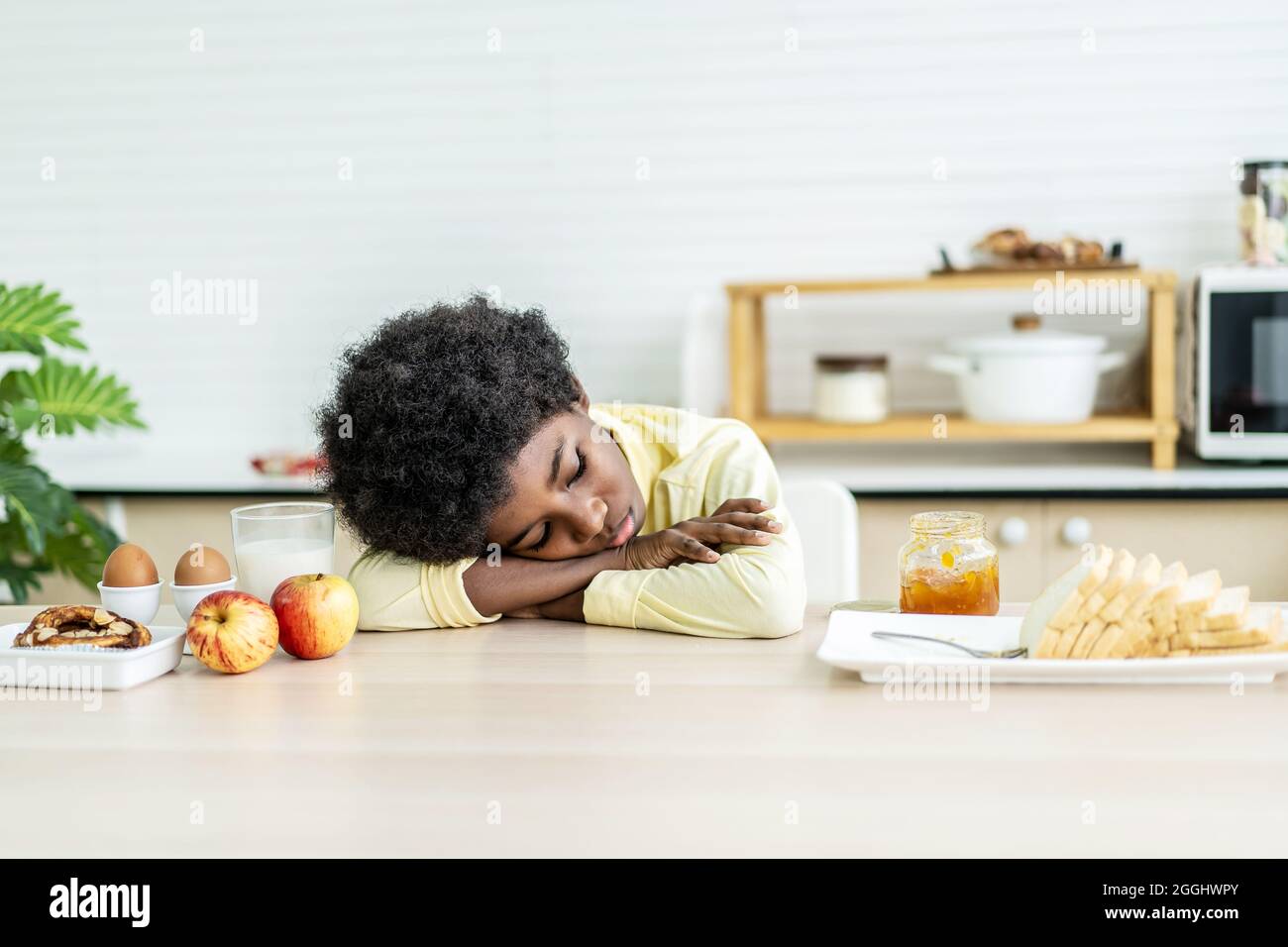 little boy is sitting at the kitchen table leaning her face in her arms ...