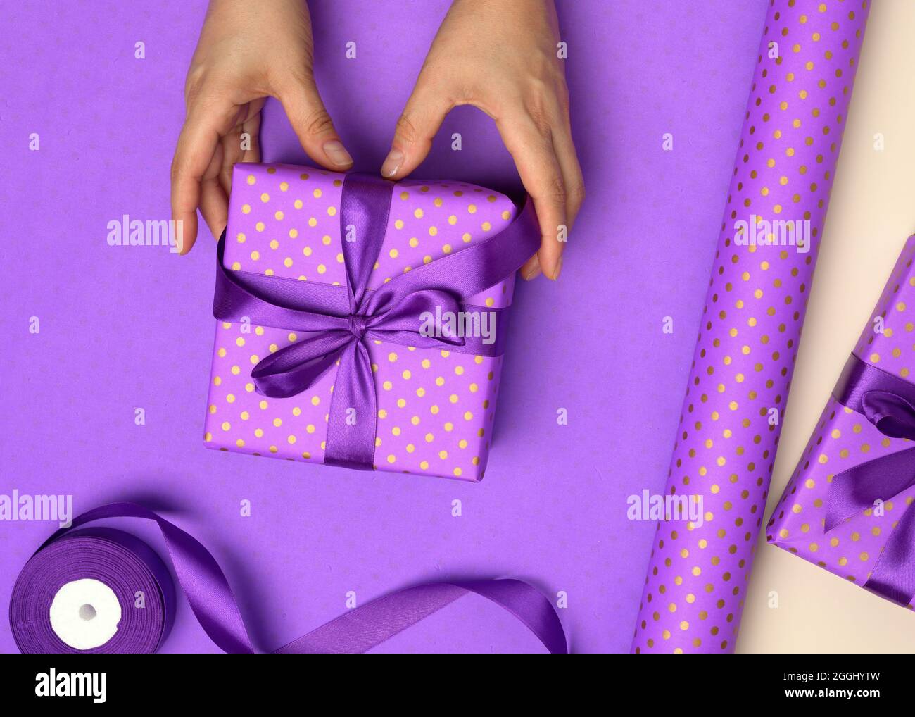 two female hands are holding purple gift box on paper background ...