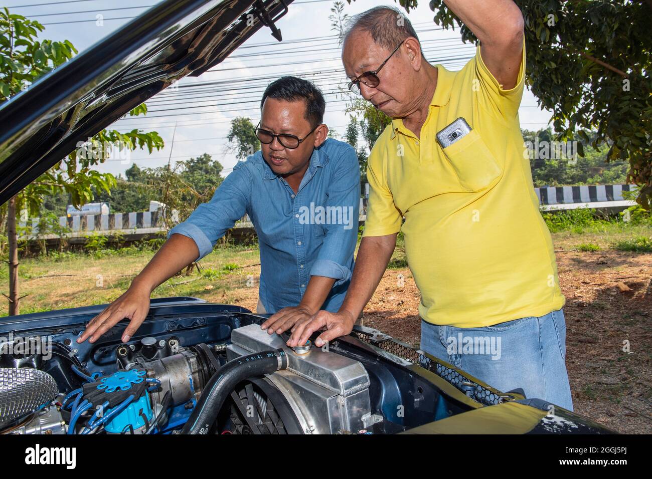 two men looking under the hood of American muscle car in Thailand Stock ...