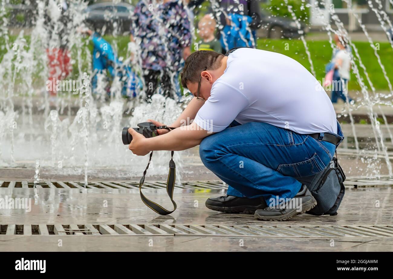 photographer is sitting and holding a digital SLR camera in a ...
