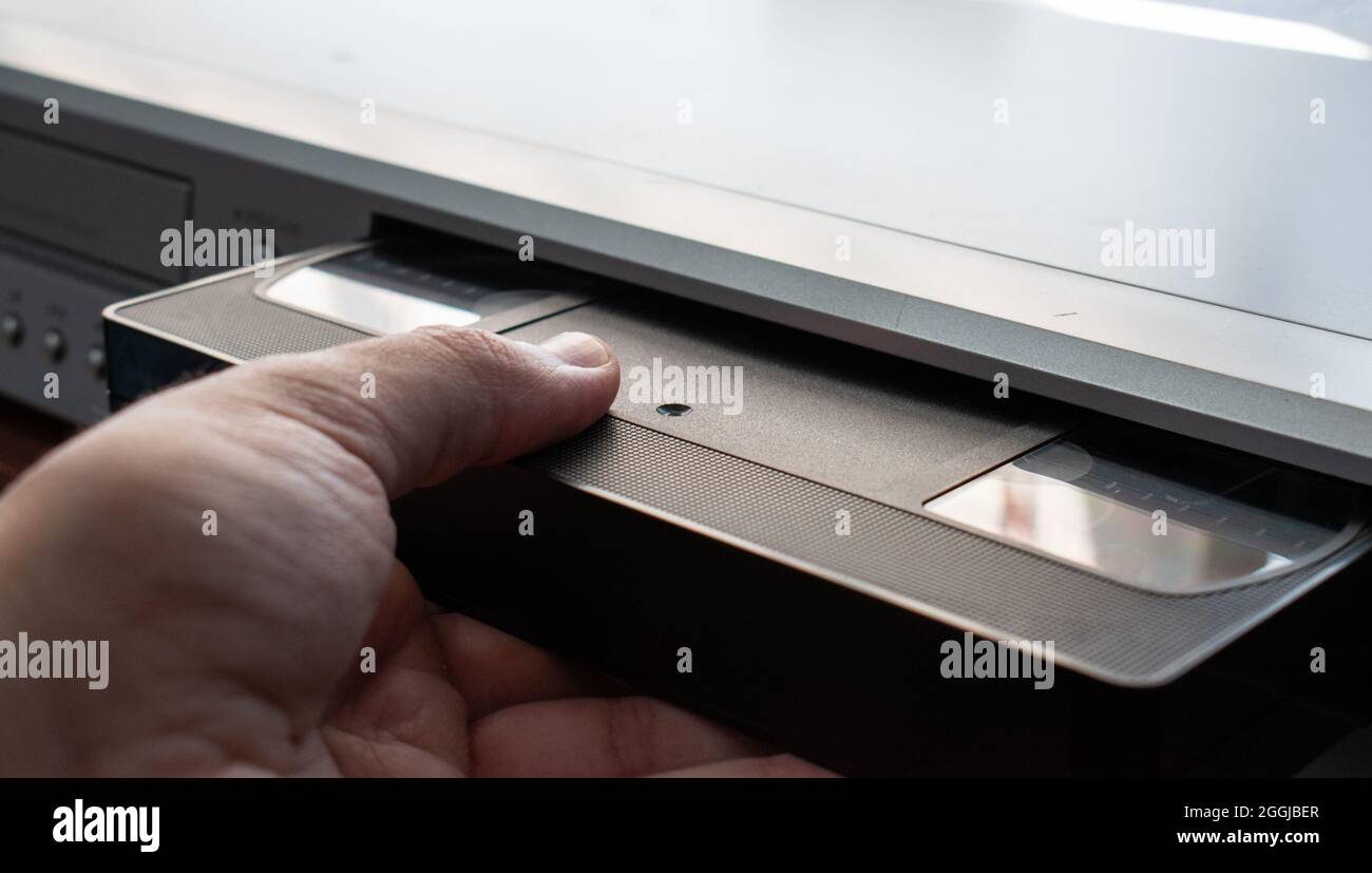 Person inserting an old VHS video cassette tape in a video recorder ...
