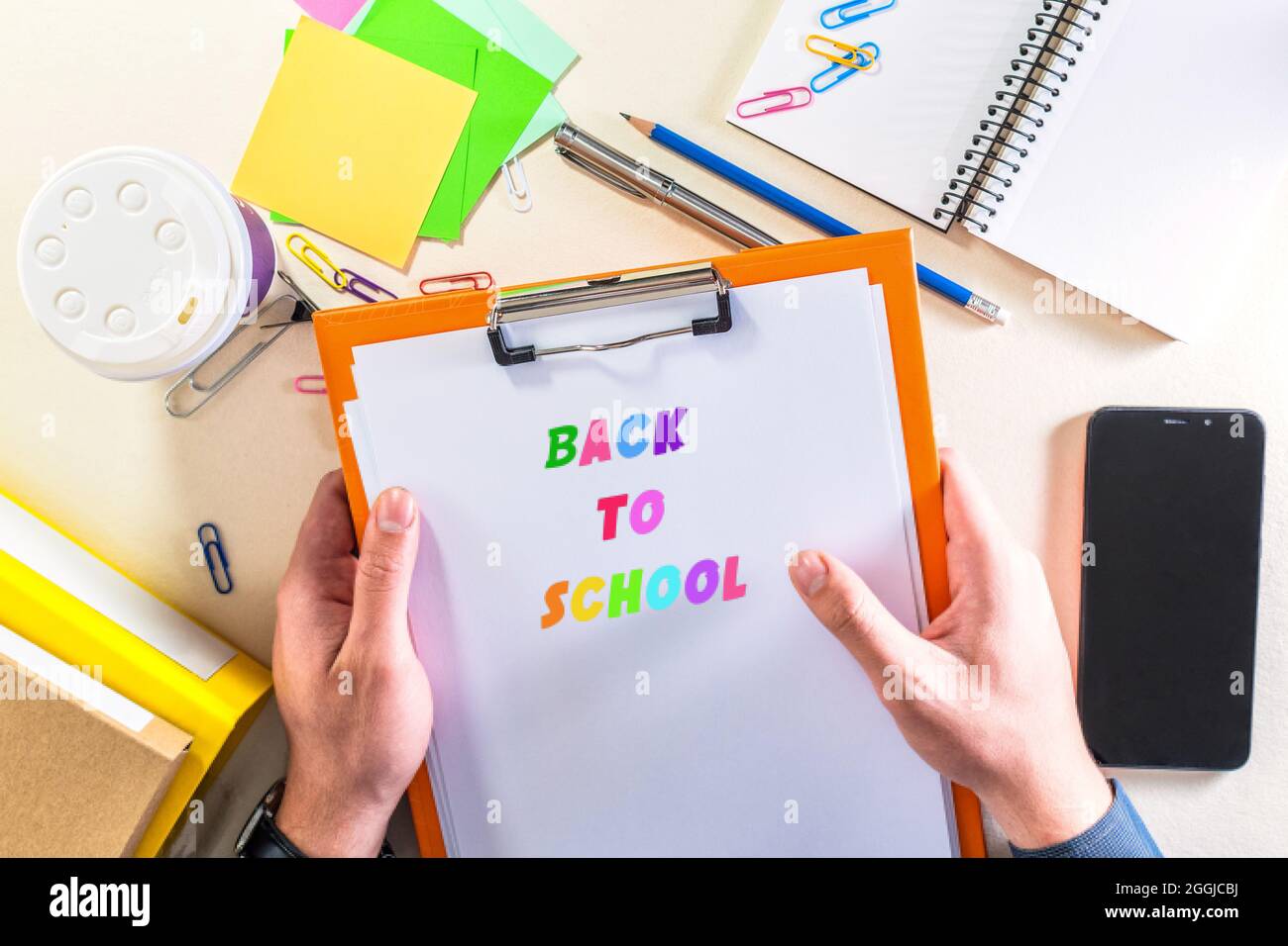 Top view of a student's hands holding a clipboard with a text ''Back to ...