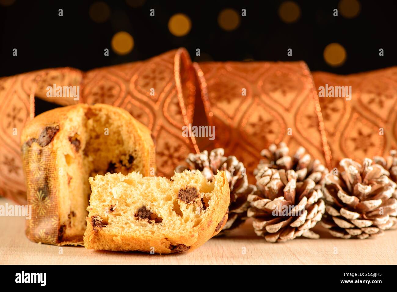 small panettone with a slice next to pine cones and decorative ribbon ...