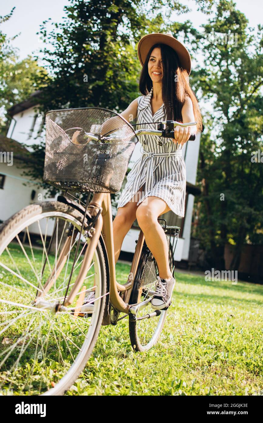 Full-length portrait of young beautiful girl riding bike in garden on ...