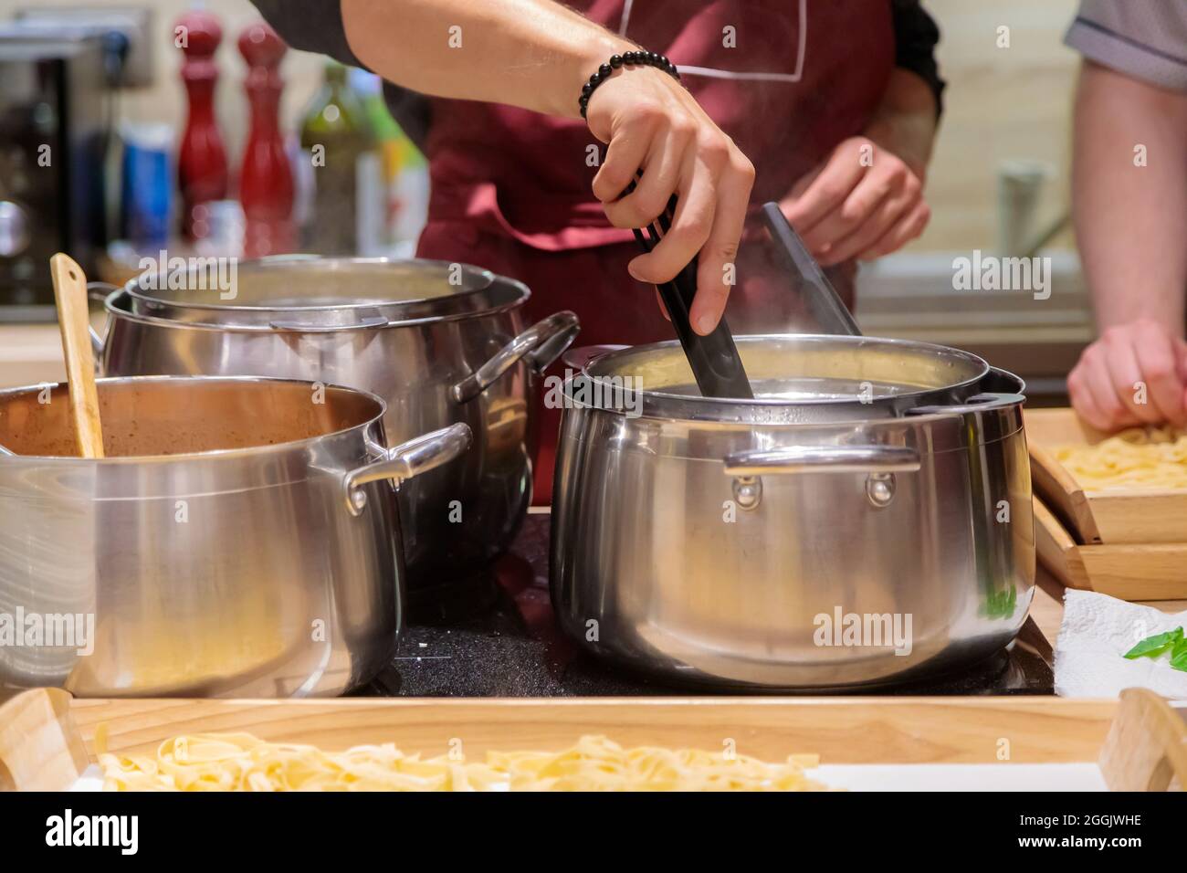 The chef prepares pasta in large metal pans. Male hands take out the ...