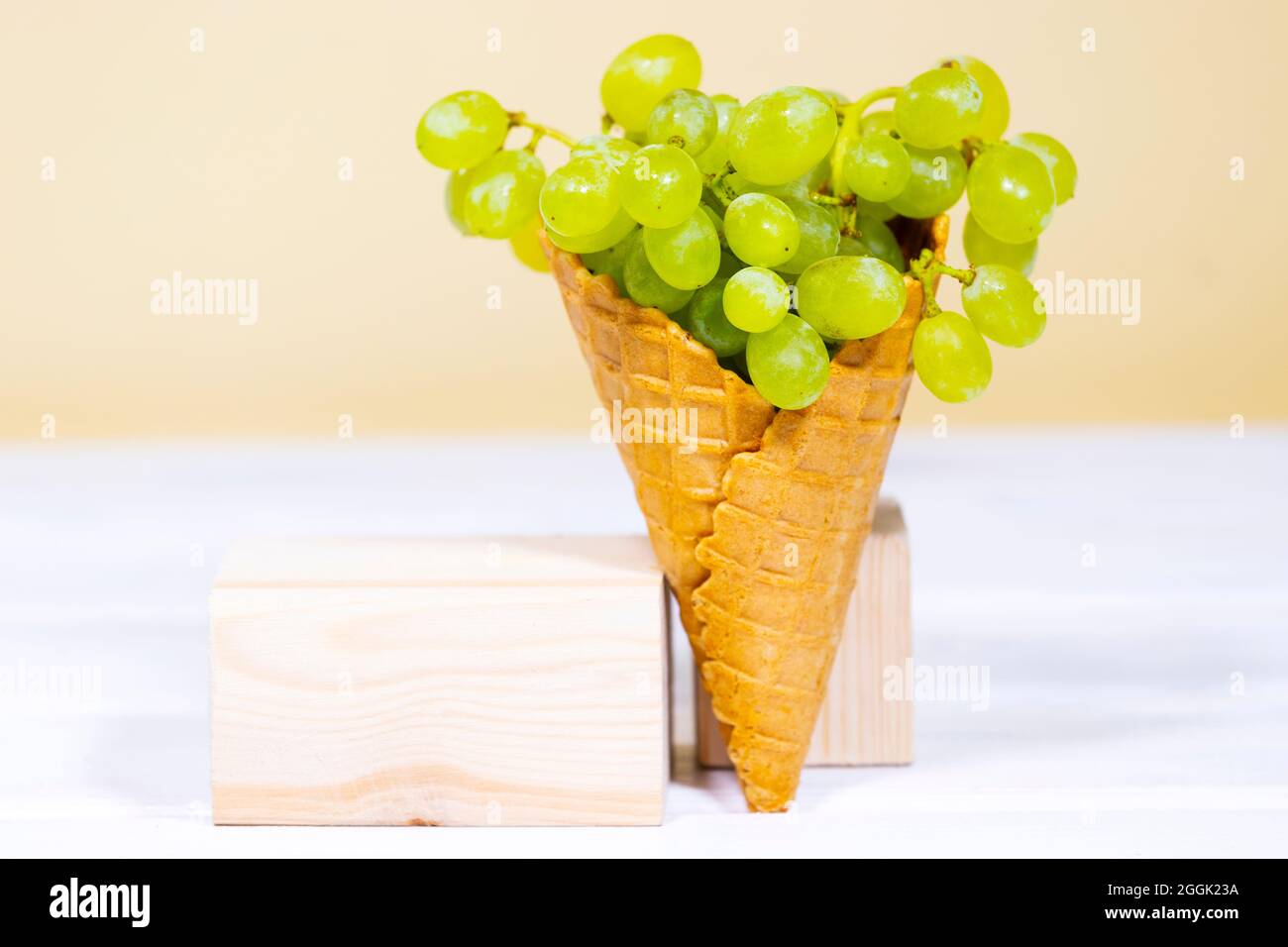 Green grape in sweet wafer cone on wooden stands over light orange ...