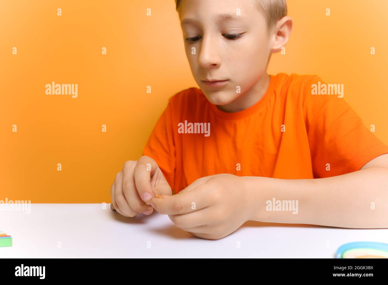 a child in an orange T-shirt tries to insert a thin strip of paper into ...