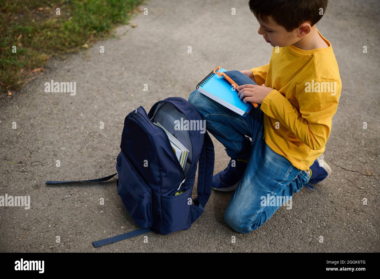 Charming elementary aged schoolboy sits on his knees on a path in the ...
