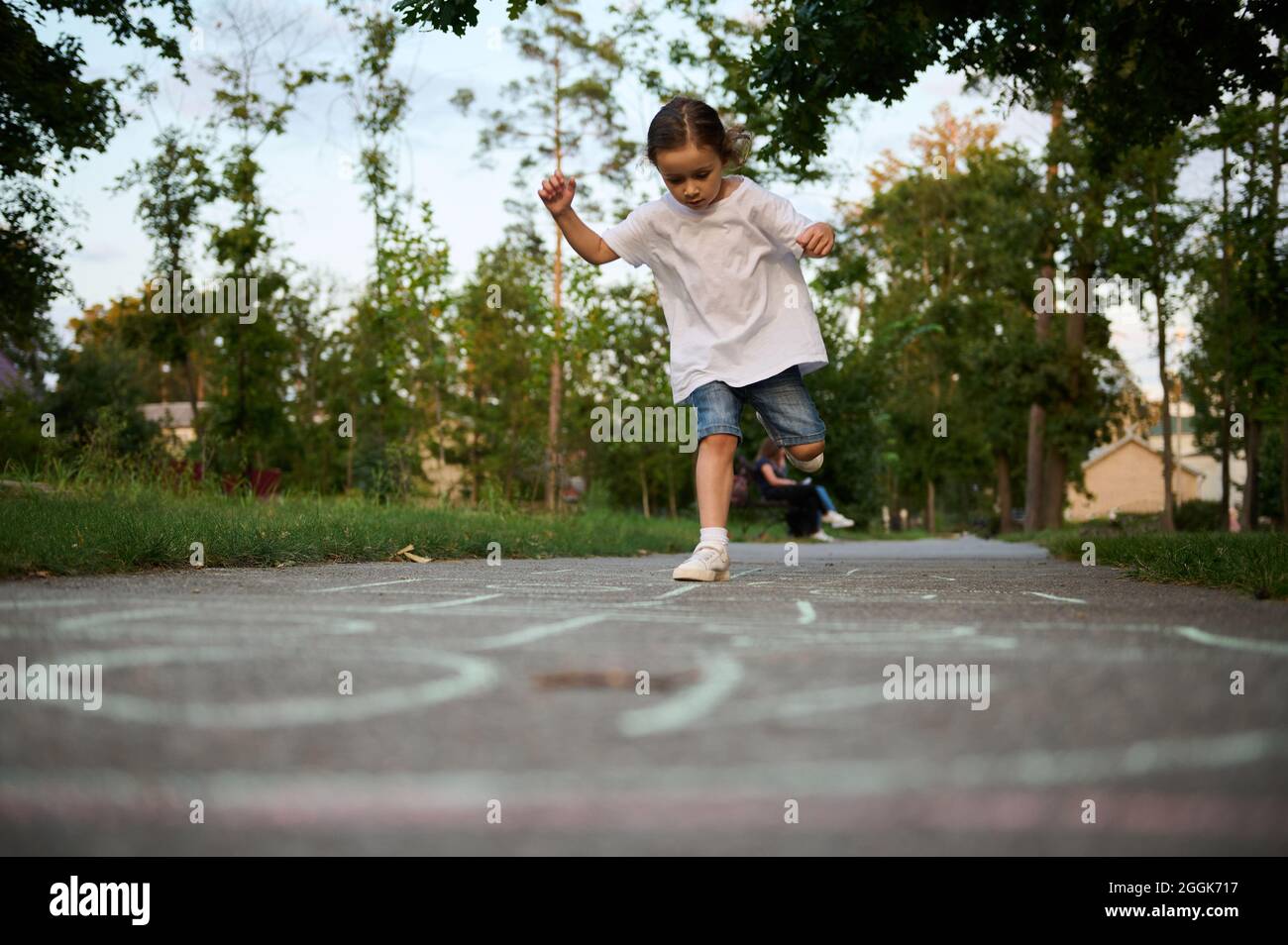 An active sporty 4 years old baby girl plays hopscotch , takes turns ...