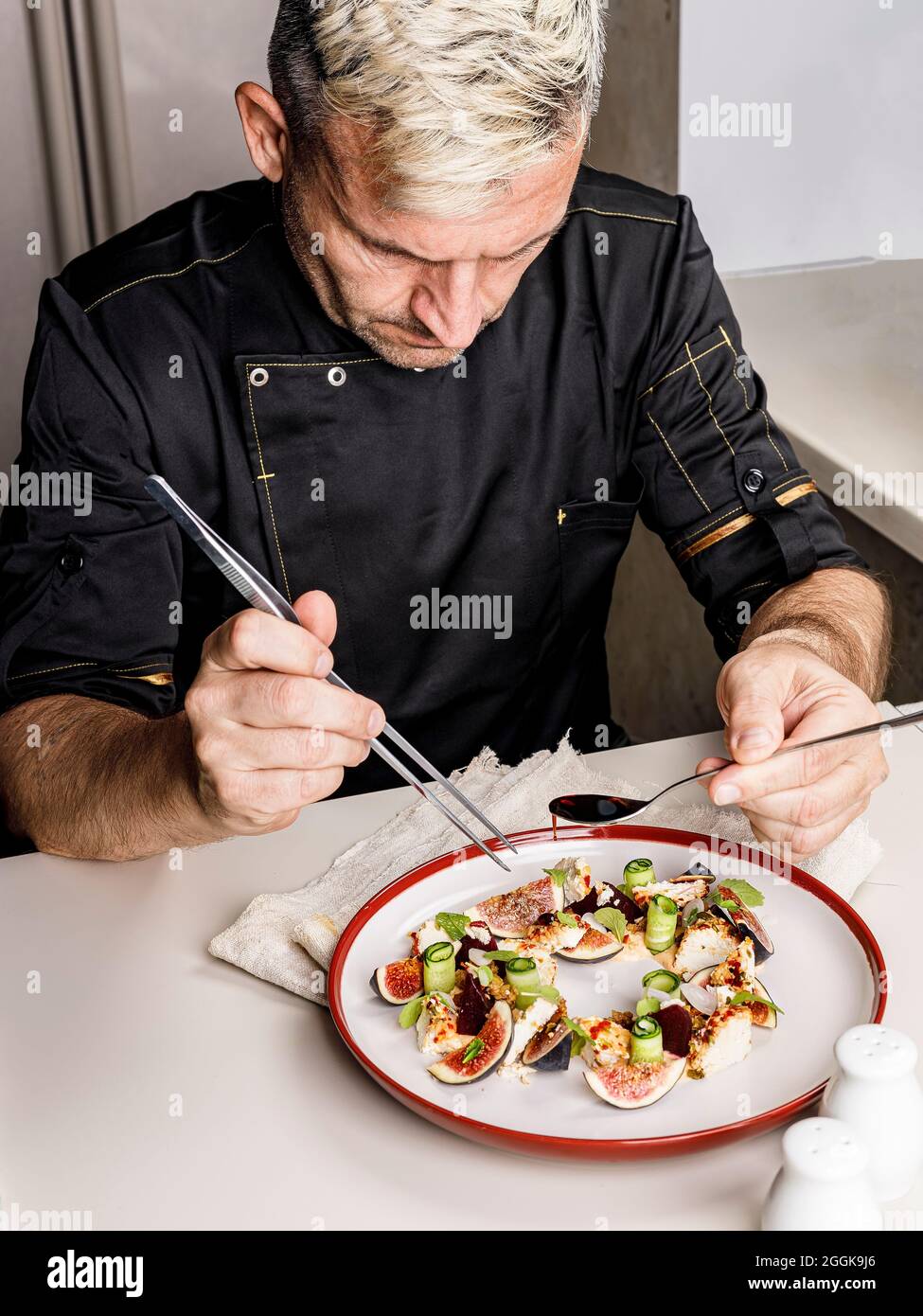 A stylish chef in a black jacket prepares tasty salad with ripe figs ...
