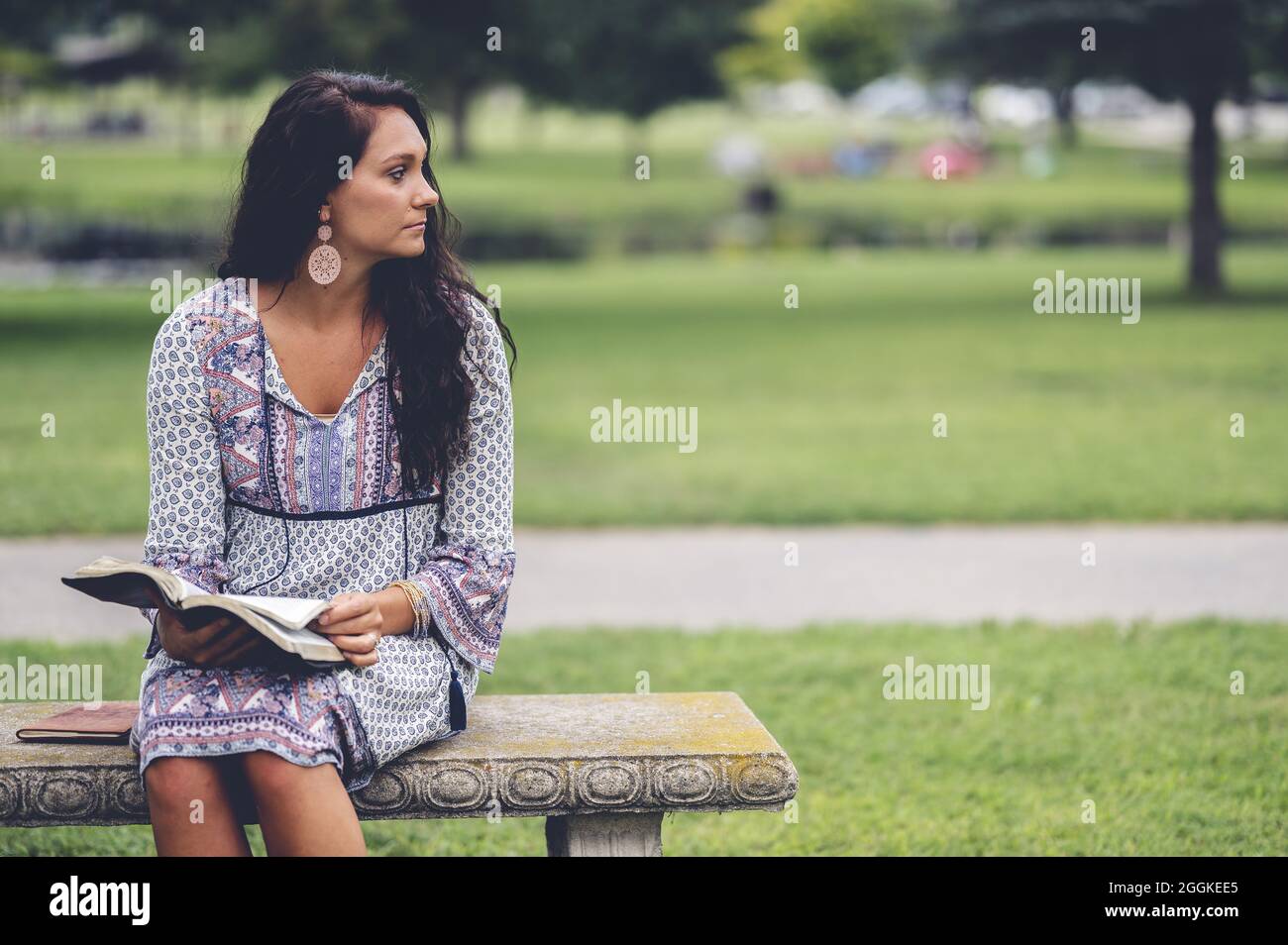 Female taking a pause from reading a bible at a park with grass and ...
