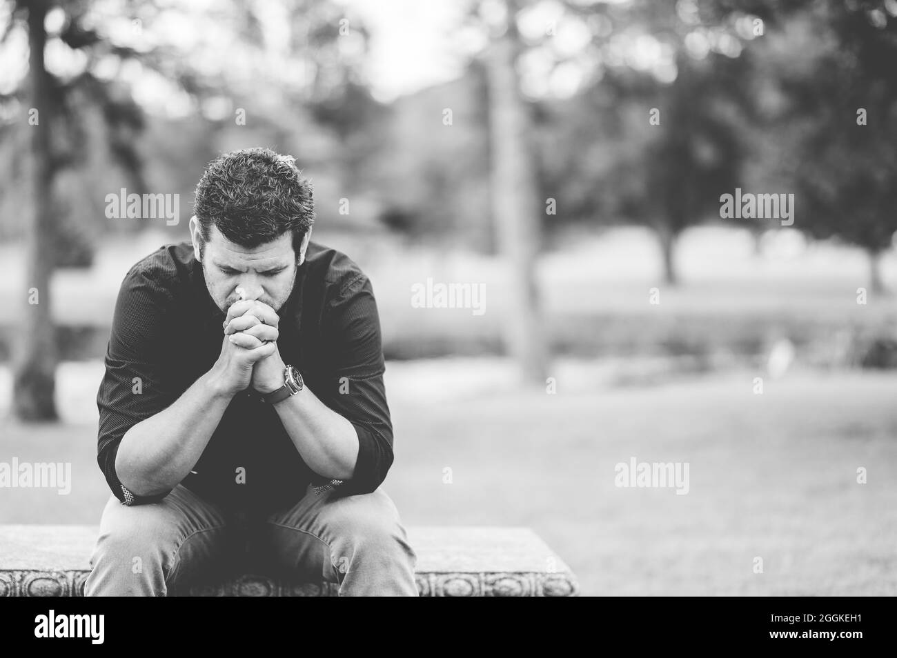 Grayscale shot of a male Caucasian praying earnestly at a park in ...