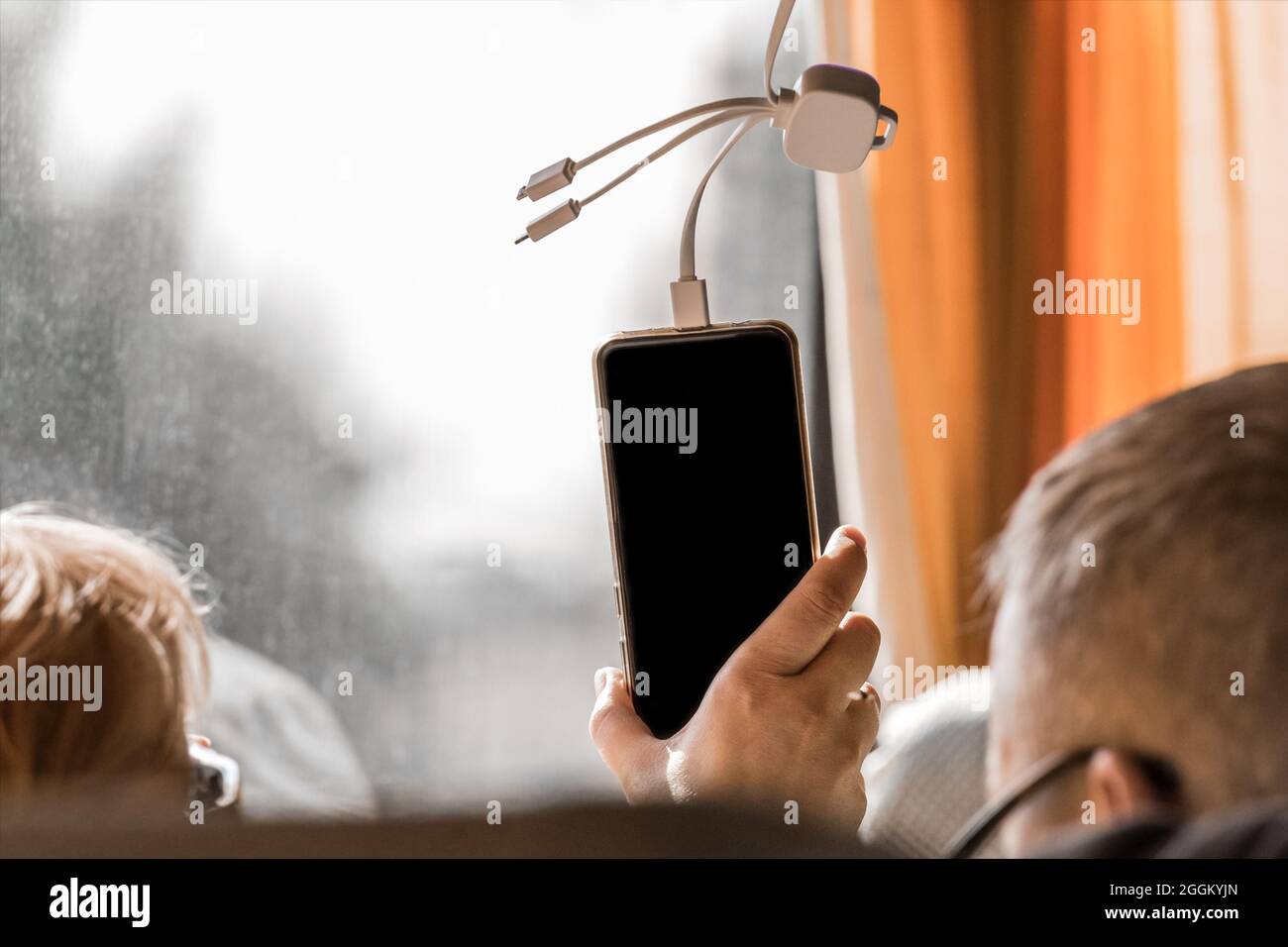 A woman holds and charges a phone on the bus using a modern USB charger ...