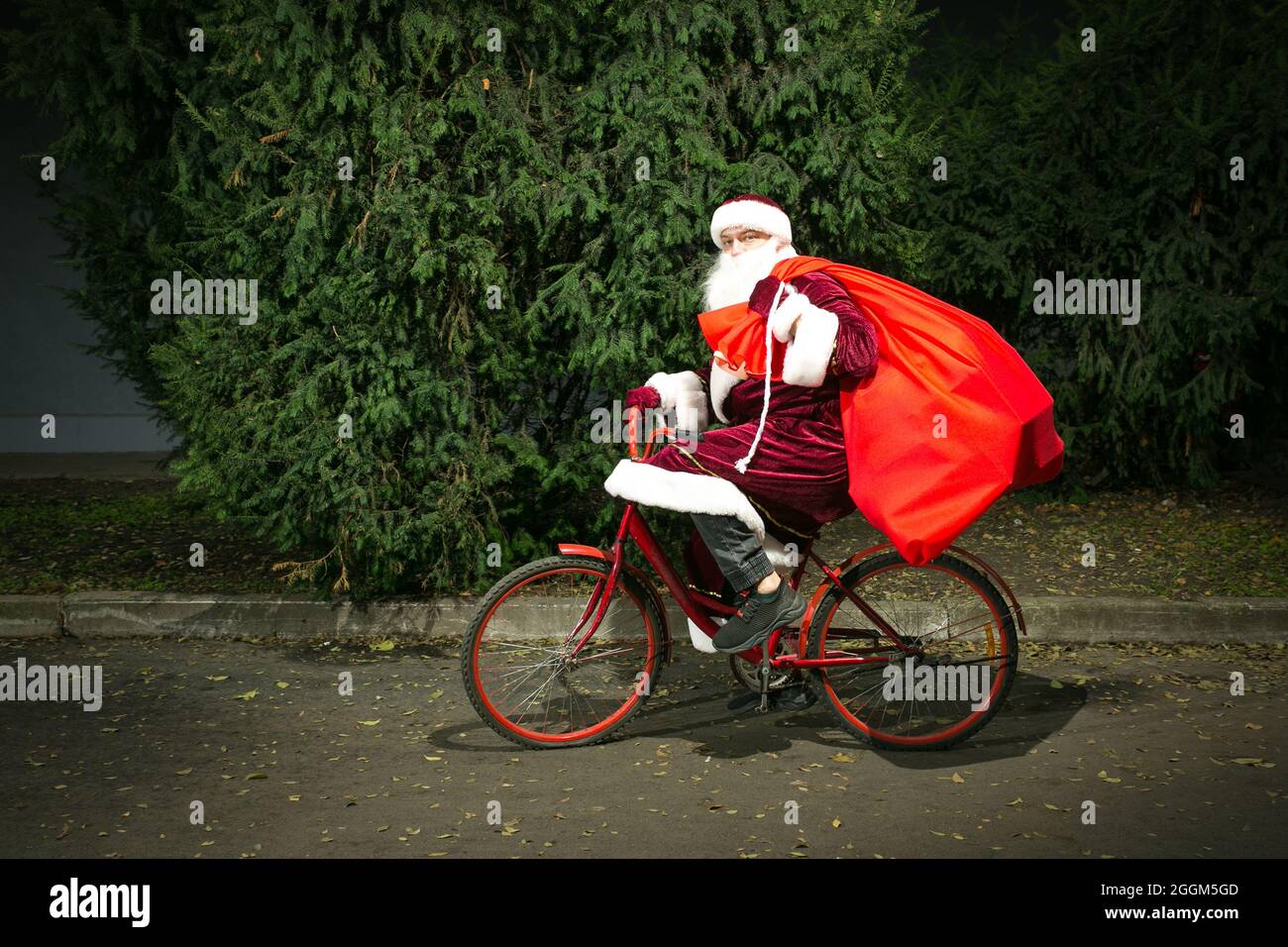 Santa Claus rides a bicycle and carries a large bag of gifts. Close-up ...