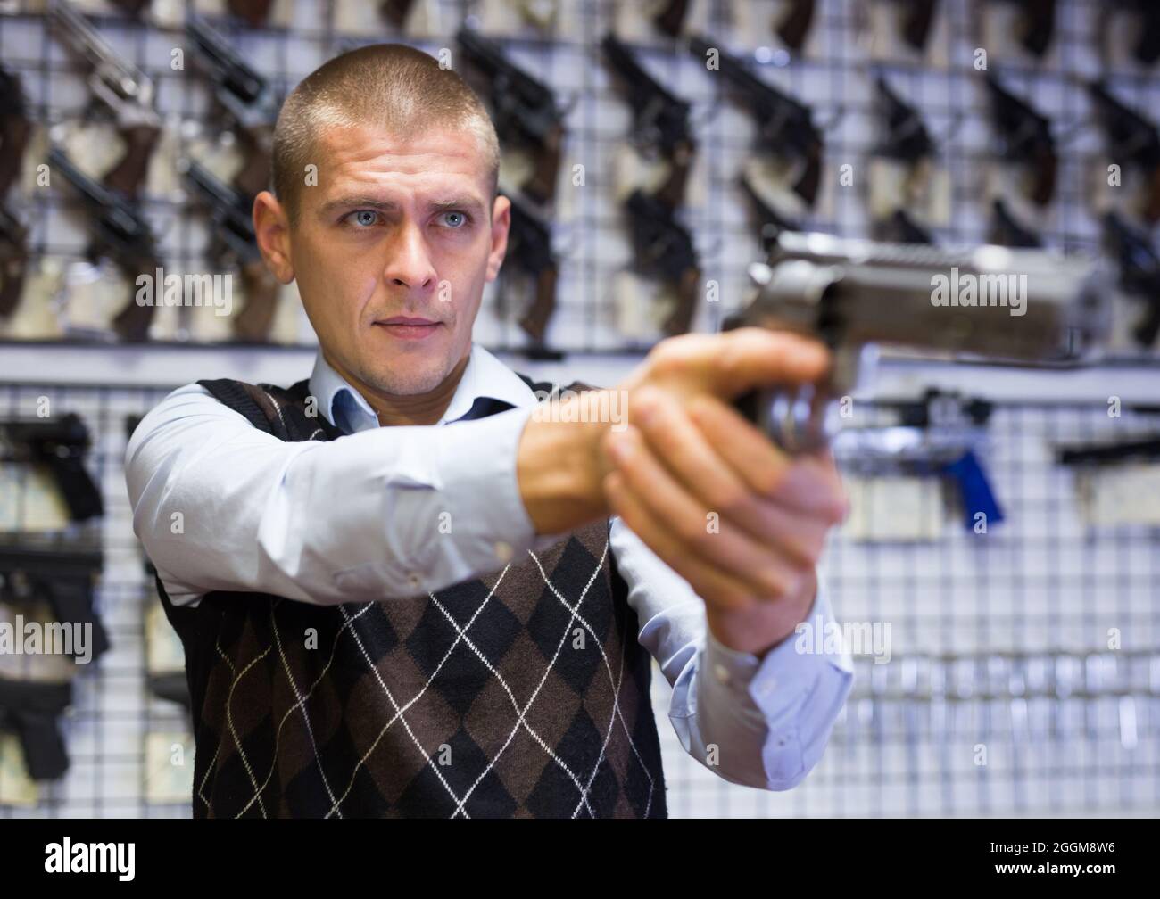 Focused man testing pistol aiming in armory shop Stock Photo - Alamy
