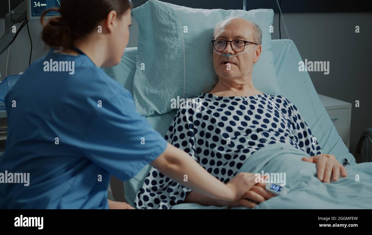 Sick old patient getting help from nurse in hospital ward for treating ...