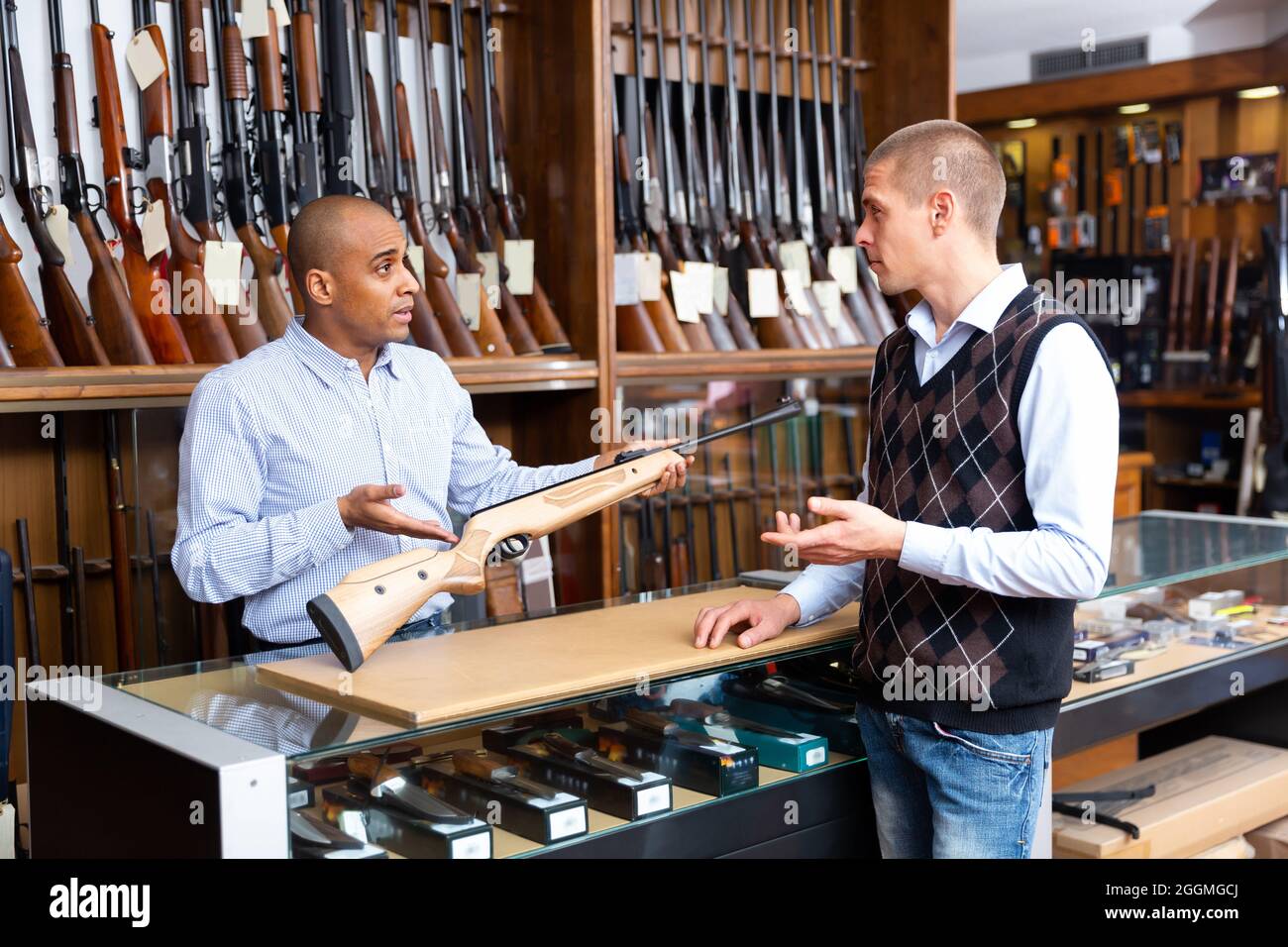 Latin american man owner of gun shop consulting customer about rifle ...
