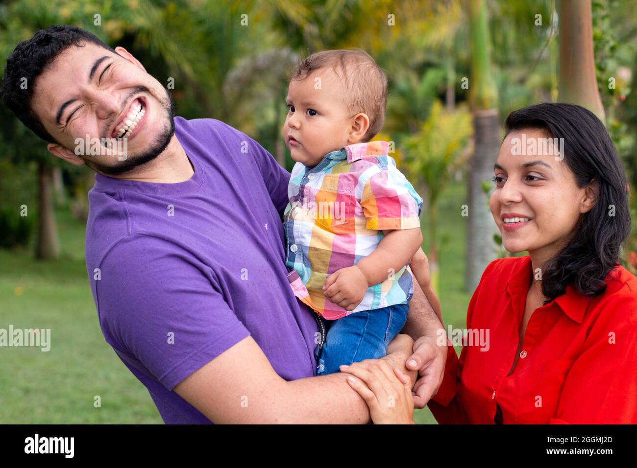 Smiling parents taking care of their baby in a beautiful park full of ...