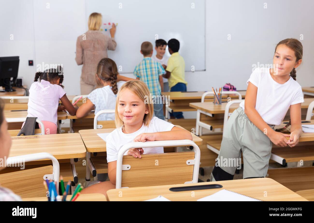 Positive primary school students are talking about homework at desk ...