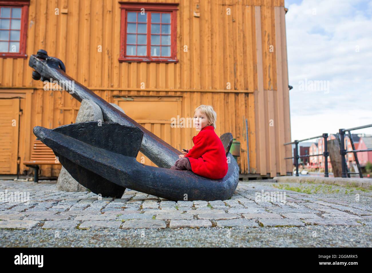 Cute blond child, sitting on a big anchor, visiting Trondheim, Norway ...