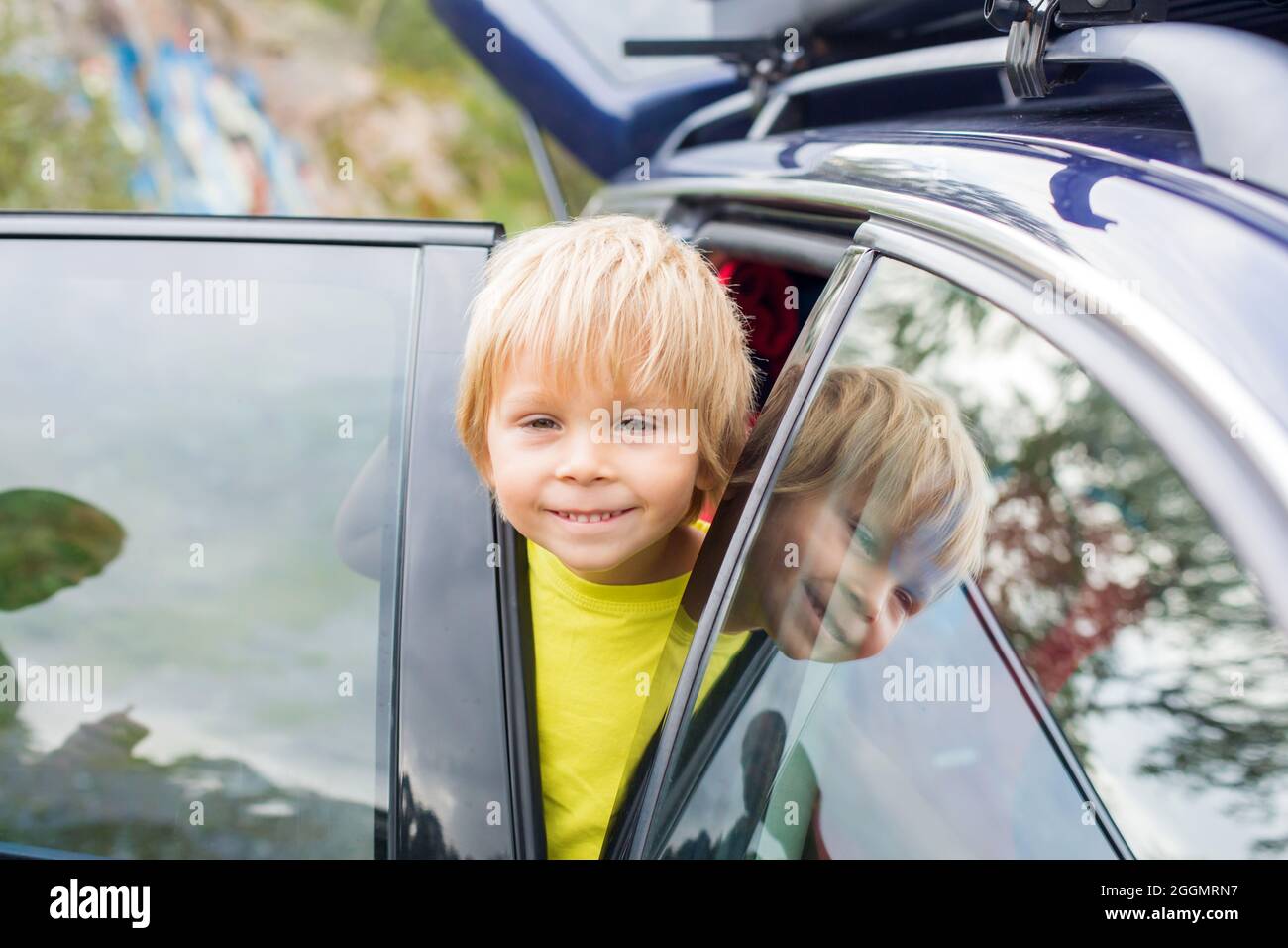 Cute blond child, looking out of the window of a car, reflection on the ...